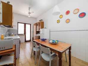 Uma cozinha com mesa de jantar, cadeiras, ventilador de teto e geladeira.