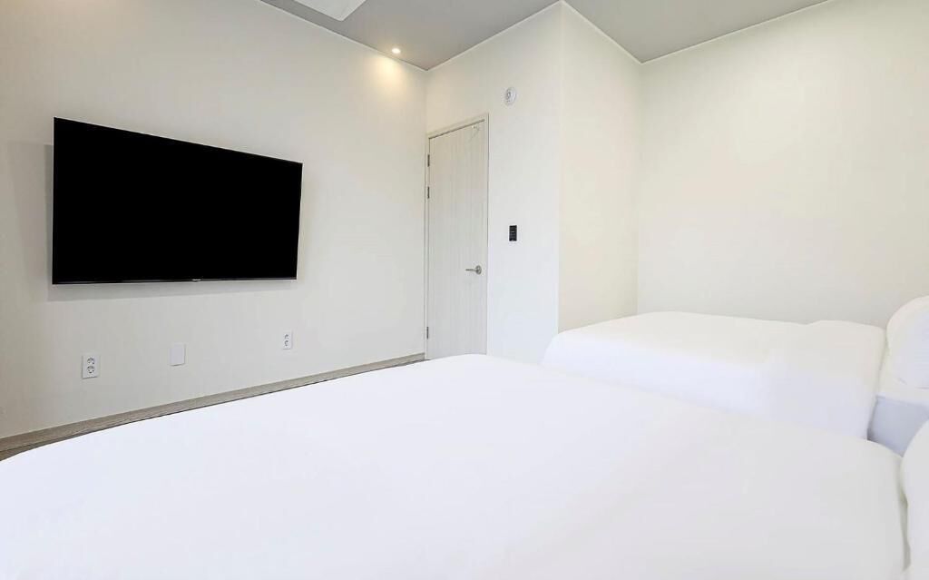 Quarto de hotel moderno com uma cama grande, televisão de tela plana na parede e uma porta.