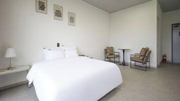 Quarto de hotel com uma cama grande, duas cadeiras, uma mesinha e três obras de arte emolduradas na parede.