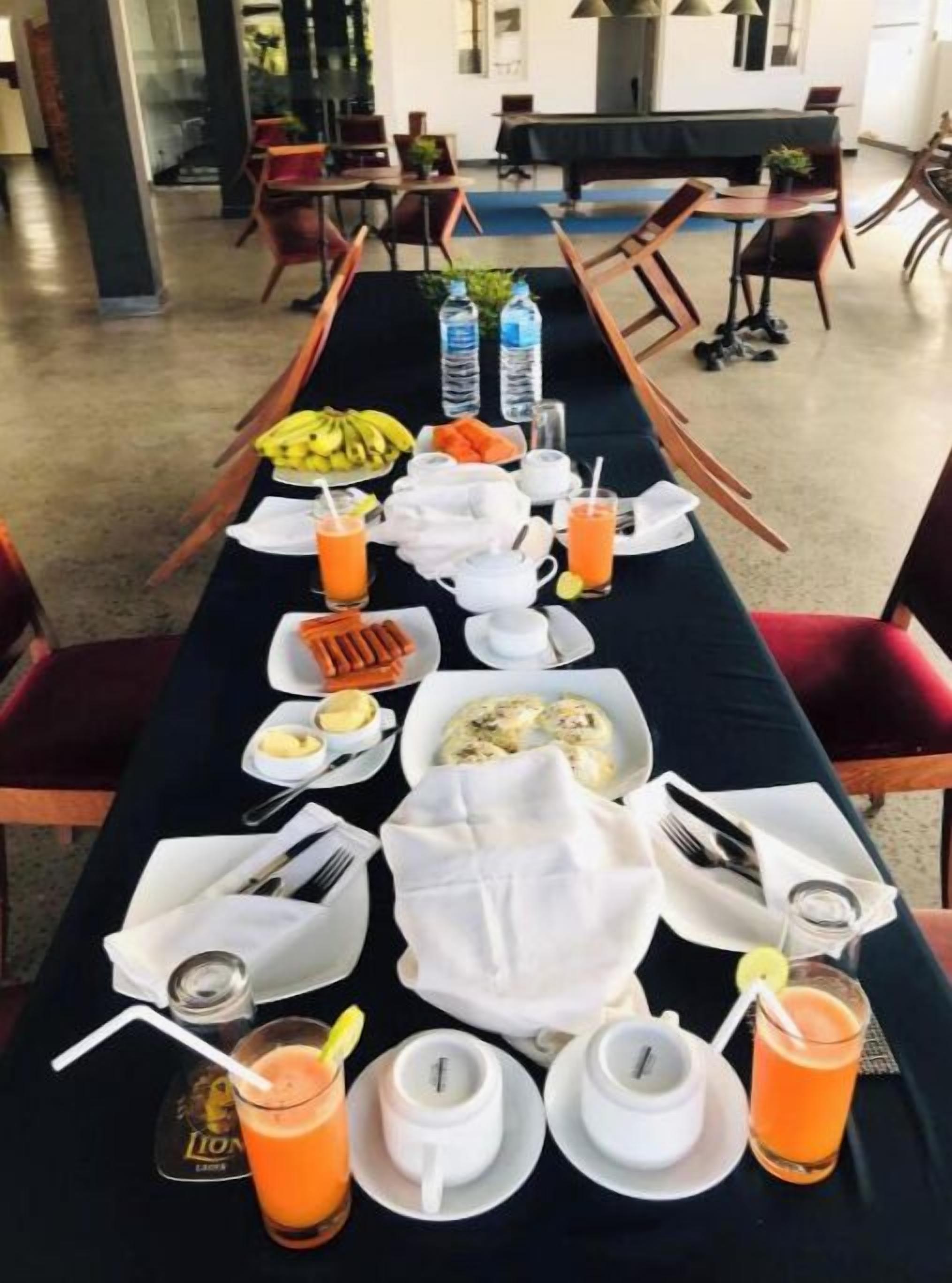 Buffet de café da manhã com diversos pratos, bebidas e utensílios para refeições.