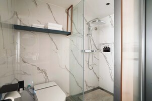 Um banheiro moderno com chuveiro envidraçado, paredes de mármore e vaso sanitário branco.