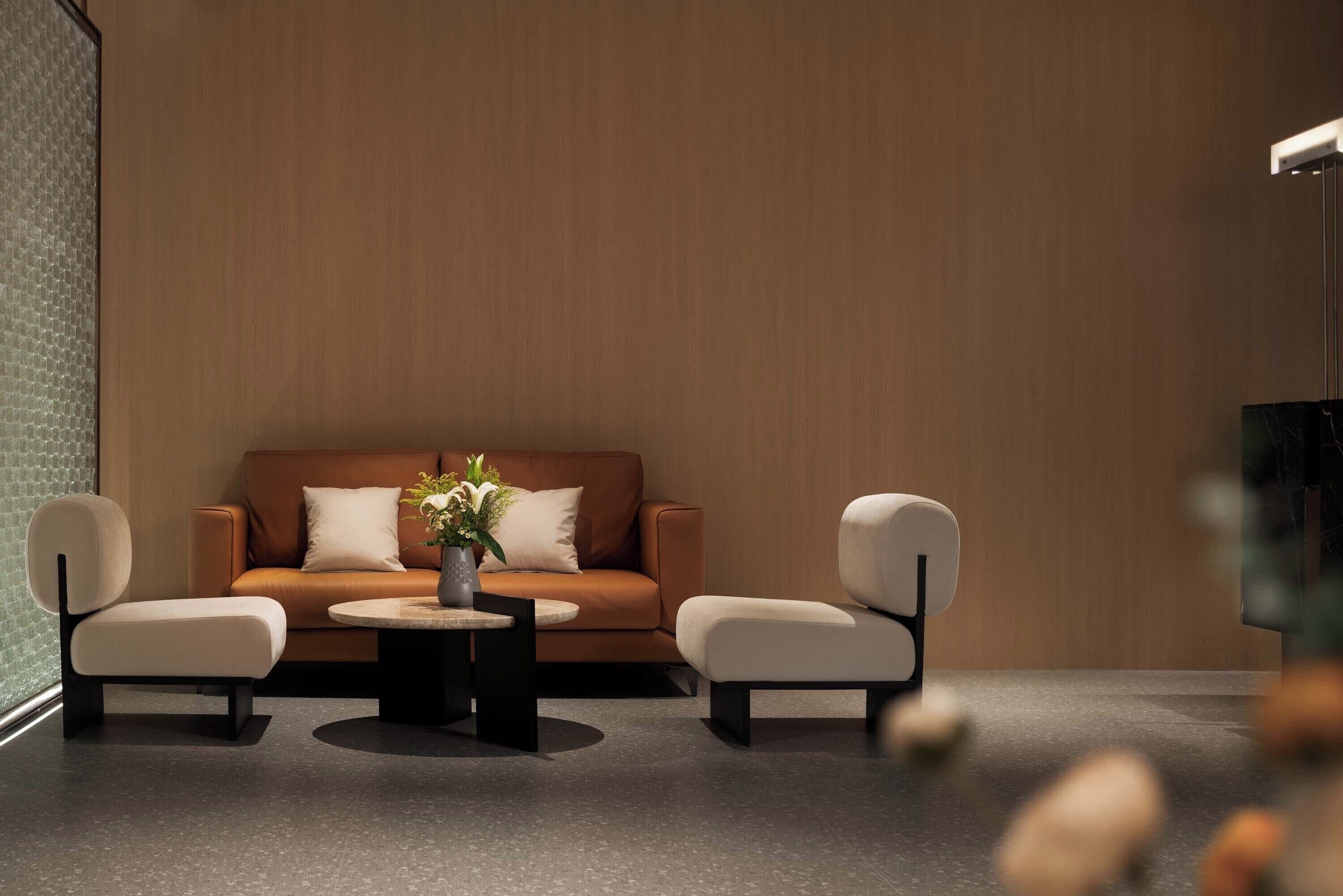 Uma sala de estar moderna com um sofá marrom, duas poltronas, uma mesa de centro e um vaso com flores.