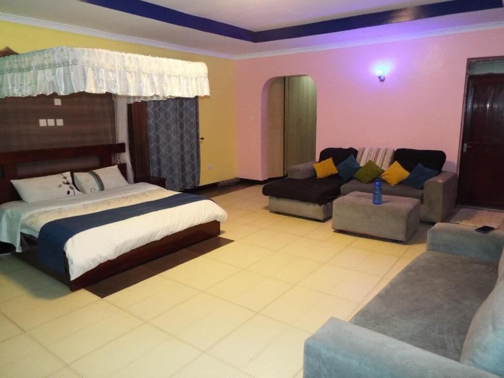 Quarto de hotel com uma cama, dois sofás, uma pequena mesa e uma porta.