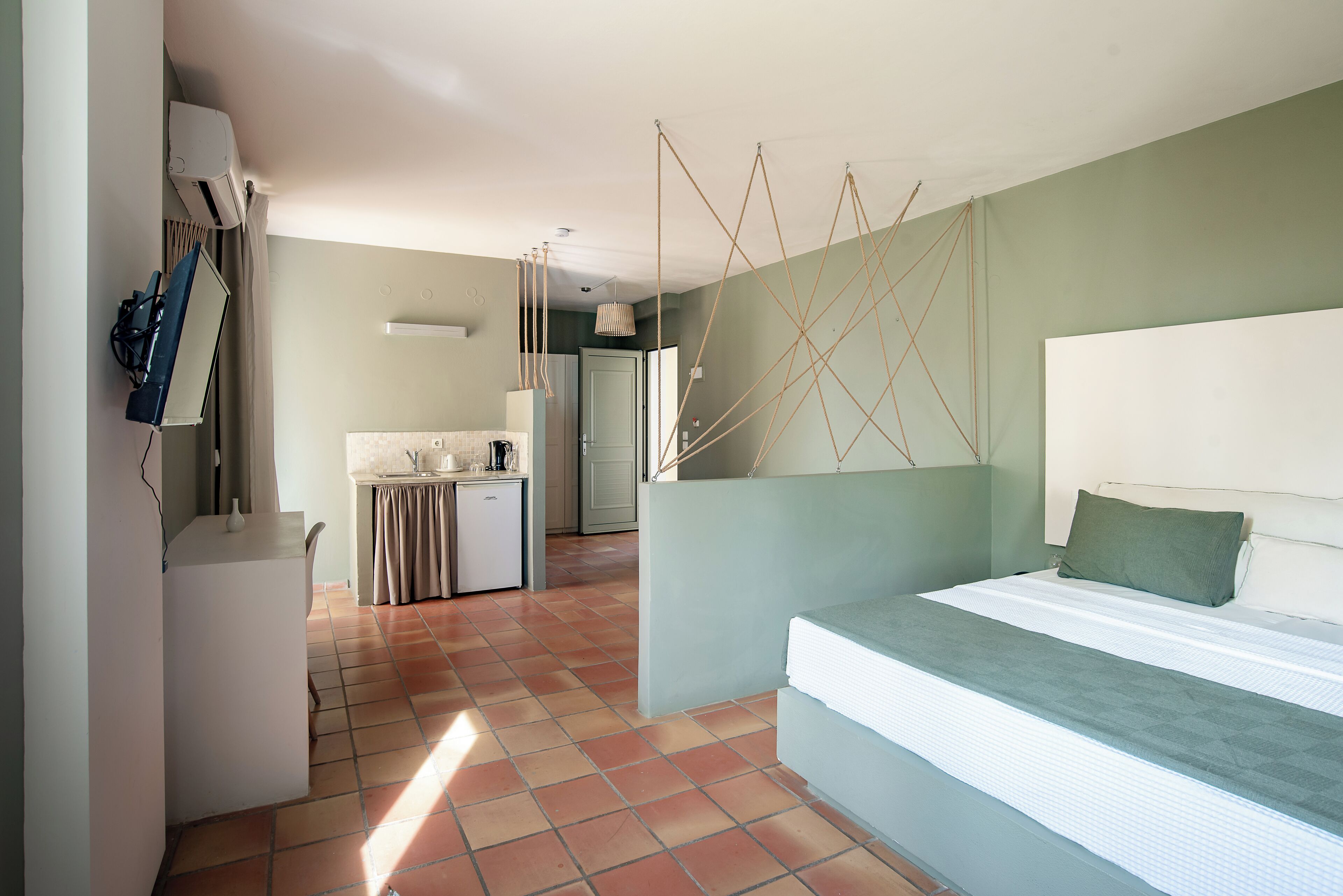 Quarto com cama, escrivaninha e cozinha compacta.