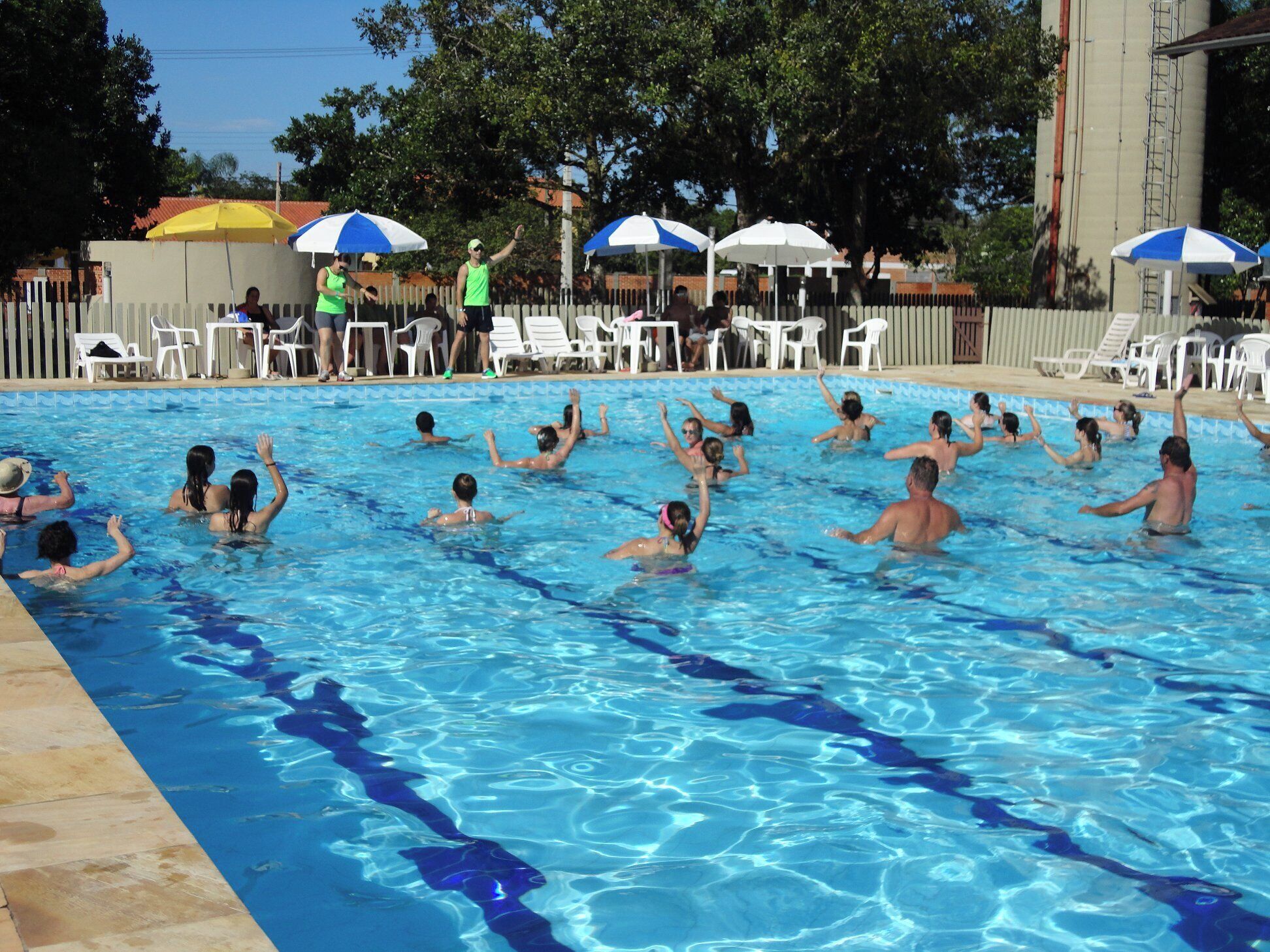 Uma piscina com água azul cristalina, rodeada por espreguiçadeiras e guarda-sóis brancos.