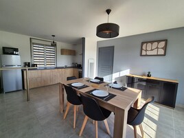 Uma cozinha moderna com área de jantar, apresentando uma mesa de madeira, cadeiras pretas e um lustre.