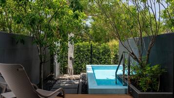 Área da piscina com deck de madeira, uma cadeira de descanso e um pequeno jardim com cerca.