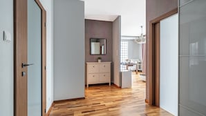 Um corredor moderno com piso de madeira, um aparador branco com gavetas e um espelho grande na parede.