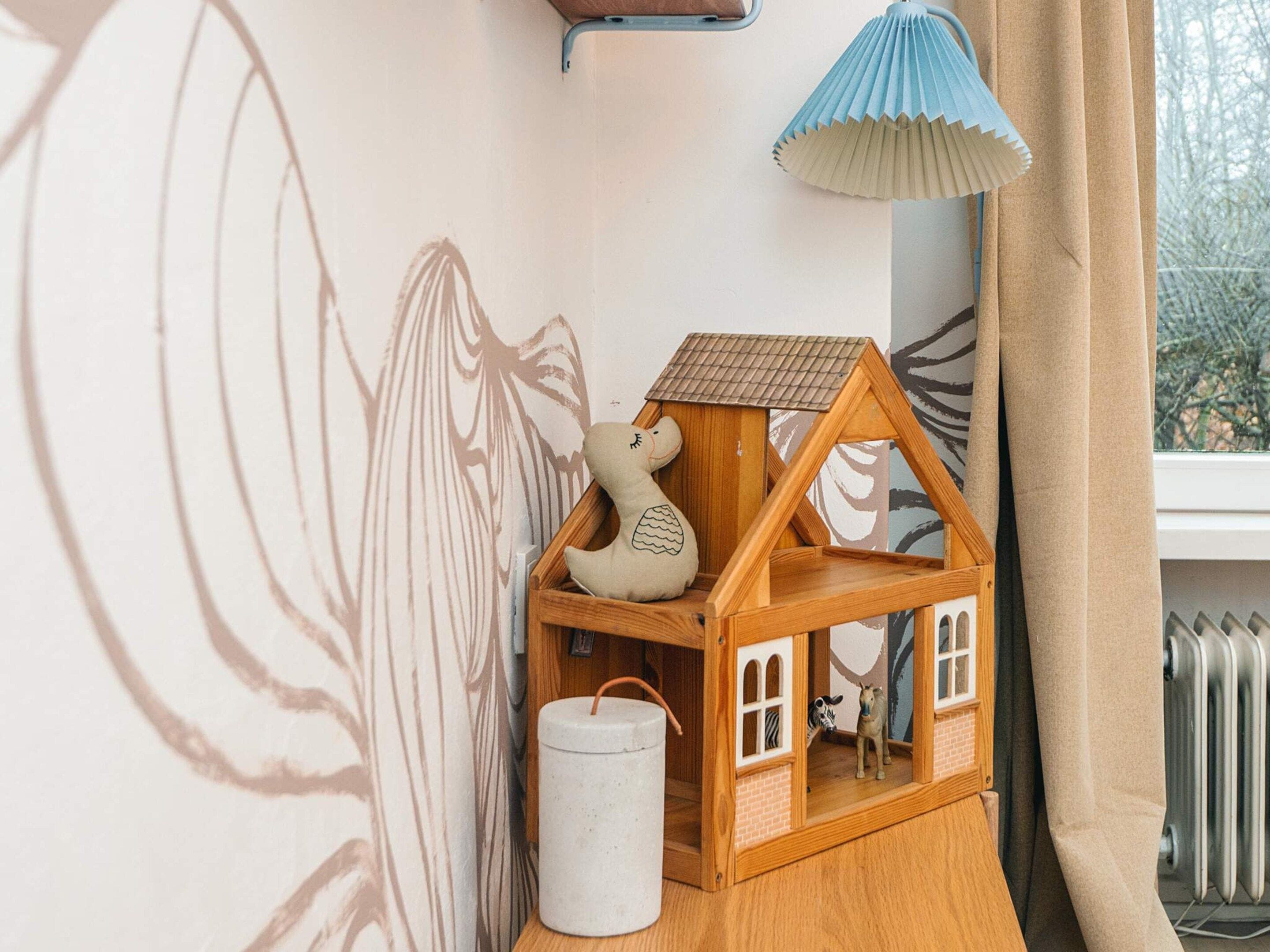 Quarto com casinha de madeira, um recipiente branco e parede com padrão de folhas.