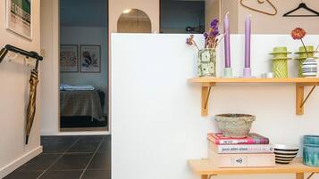 Um corredor com uma cama, um quadro branco e prateleiras com livros e velas.