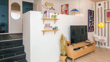 Uma sala de estar moderna com televisão, estantes de madeira, uma planta e uma escada.