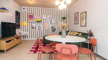 Uma sala de estar moderna com uma mesa de jantar redonda, cadeiras laranja, parede listrada e diversas obras de arte emolduradas.