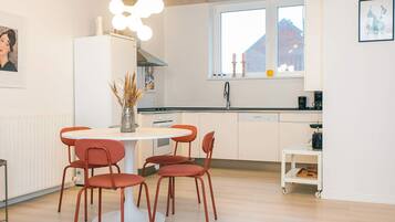 Cozinha moderna com mesa de jantar redonda e quatro cadeiras, janela com vista para um edifício e luminária pendente.