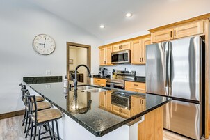 Uma cozinha moderna com ilha central, eletrodomésticos de aço inoxidável, armários de madeira e um relógio de parede.