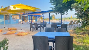 Uma área externa com mesas, cadeiras, piscina e guarda-sóis.