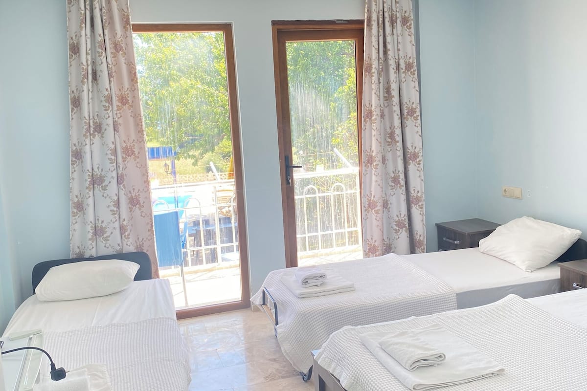 Quarto de hotel com duas camas, uma mesa e uma janela com cortinas.