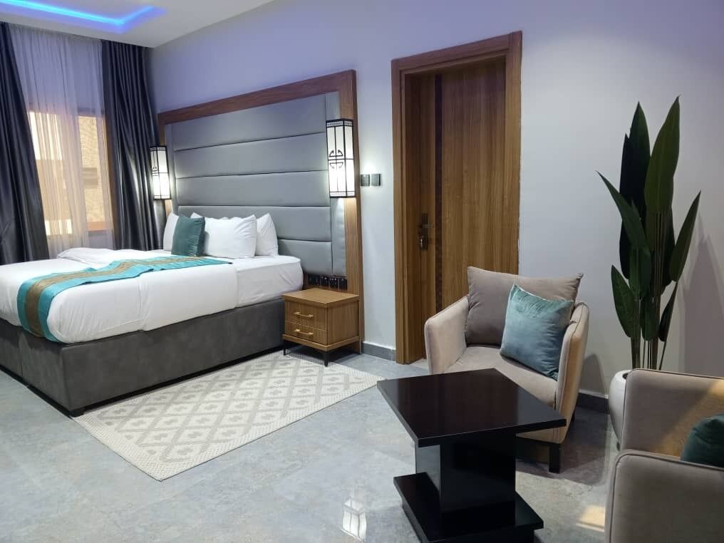 Quarto de hotel moderno com uma cama grande, mesas de cabeceira, um sofá, uma mesa de centro e um vaso de plantas.