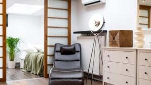 Quarto moderno com cadeira de massagem, luminária de pé, cômoda e radiador.