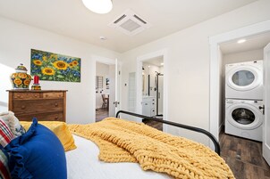 Quarto com cama, cômoda de madeira, quadro e espaço para lavanderia com máquina de lavar.