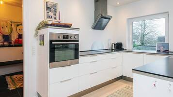 Uma cozinha moderna com forno embutido, armários brancos, uma janela com vista e um quadro na parede.