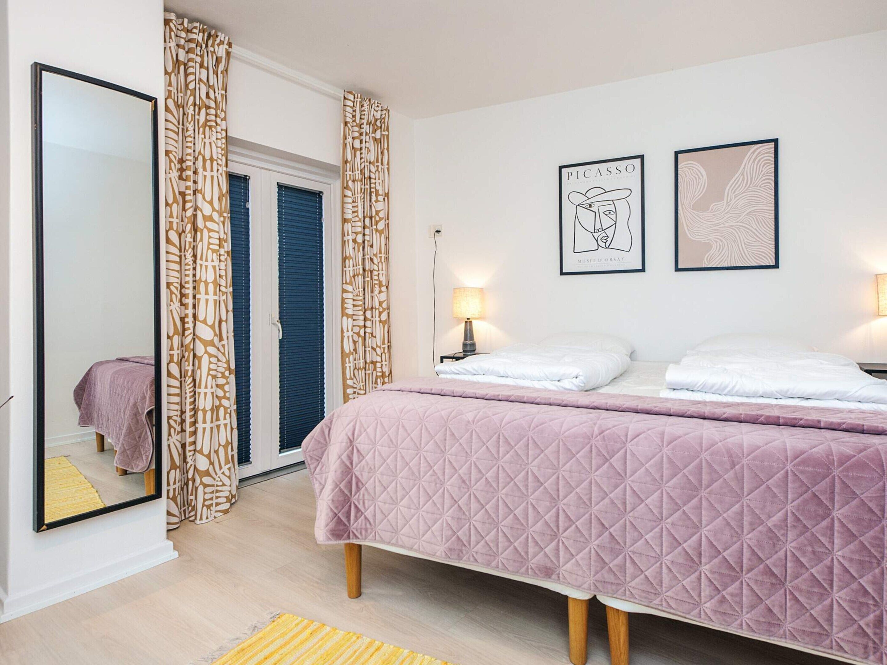 Um quarto com cama, espelho e obras de arte na parede.