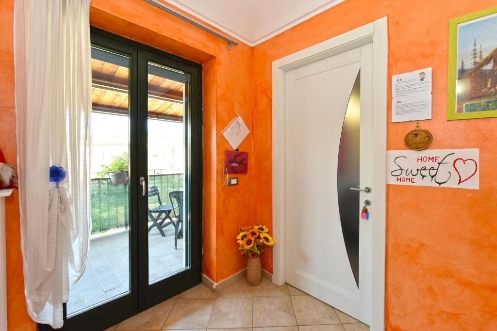 Quarto com paredes laranja, porta branca e porta de vidro deslizante para área externa com pátio e cadeiras.