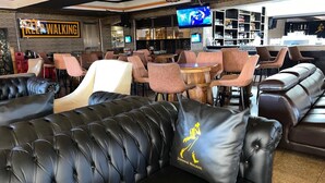 Uma área de bar com sofás de couro, um aviso com a frase 'SIGA EM FRENTE' e uma tela de televisão.
