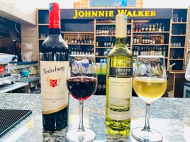 Um bar com uma garrafa de Nederburg Cabernet Sauvignon, uma garrafa de Drostdy Hof Premier Grand Cru e duas taças de vinho.