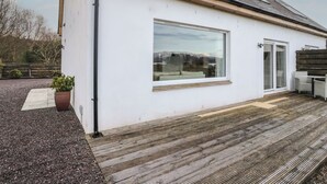 Um edifício branco com uma janela grande e uma porta, um deck de madeira e um vaso de planta.