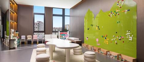 Uma área de recreação infantil moderna, com uma mesa grande e assentos, uma parede de blocos LEGO e vista para edifícios.