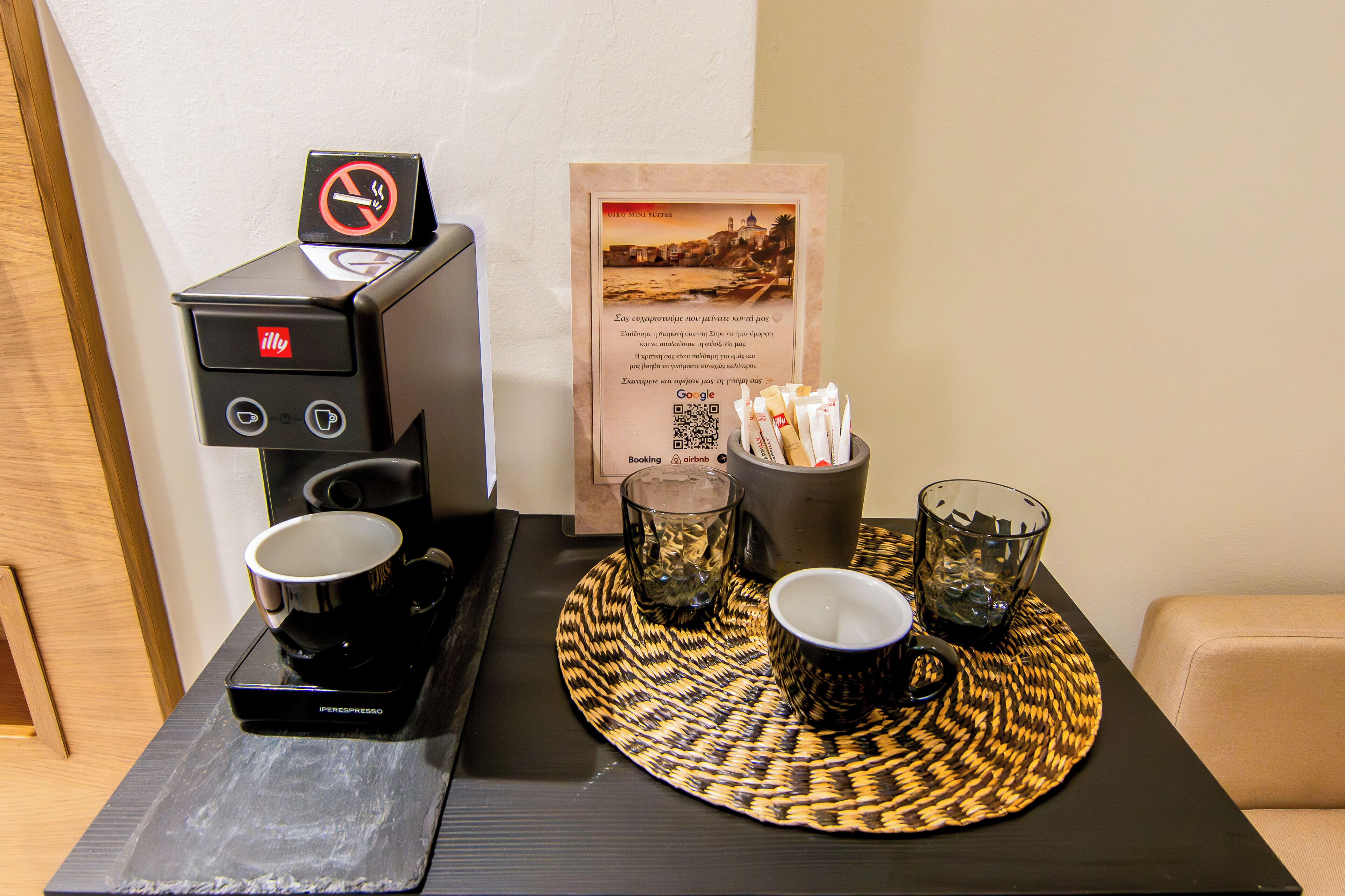 Máquina de café, duas chávenas, código QR e placa de proibido fumar sobre uma mesa.