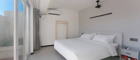 Quarto moderno com uma cama grande, uma mesa de cabeceira, um ventilador de teto, um aparelho de ar condicionado e uma porta de vidro deslizante para uma varanda externa.
