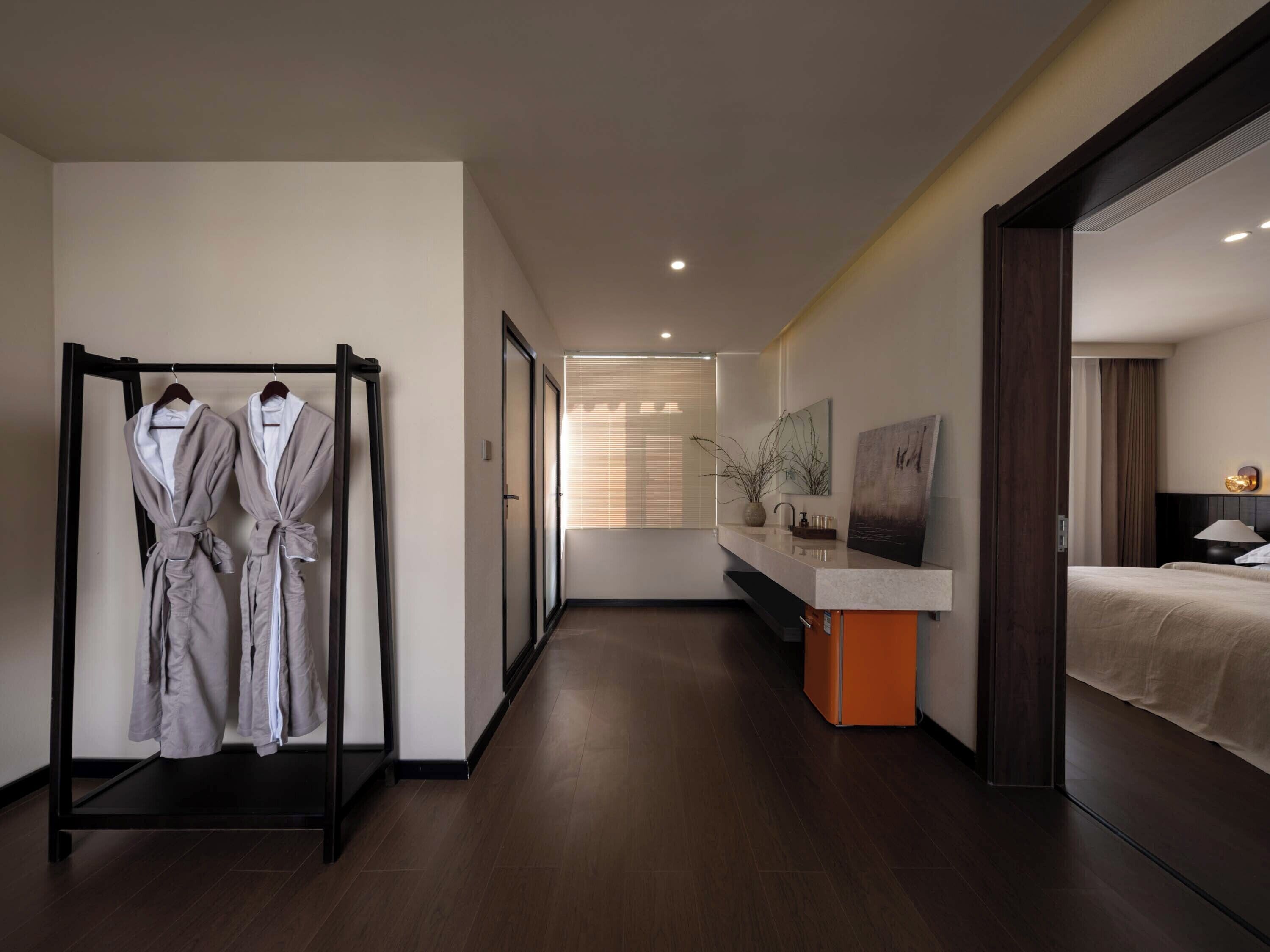 Quarto de hotel com cama, toucador com espelho e suporte para roupões com dois roupões.