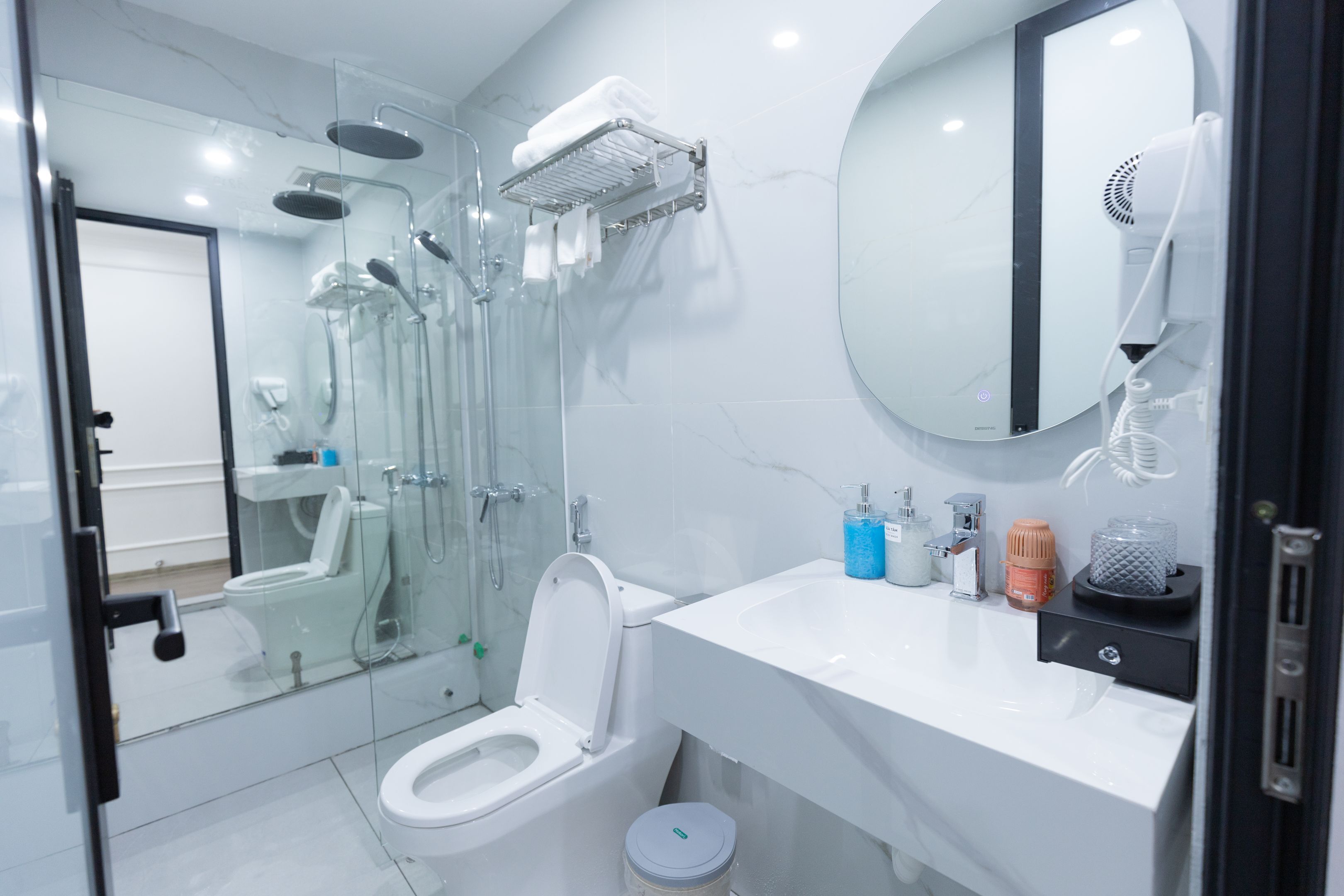 Uma casa de banho moderna com chuveiro envolto em vidro, sanita branca, lavatório com artigos de higiene pessoal e espelho.
