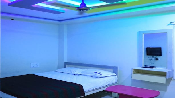 Quarto com cama, ventilador de teto, televisão e uma pequena mesa.