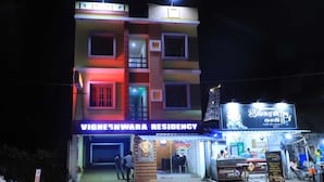 Um edifício com uma placa indicando "VIGNESHWARA RESIDENCY" e uma placa com a palavra "ROOMS", sinalizando um hotel residencial.