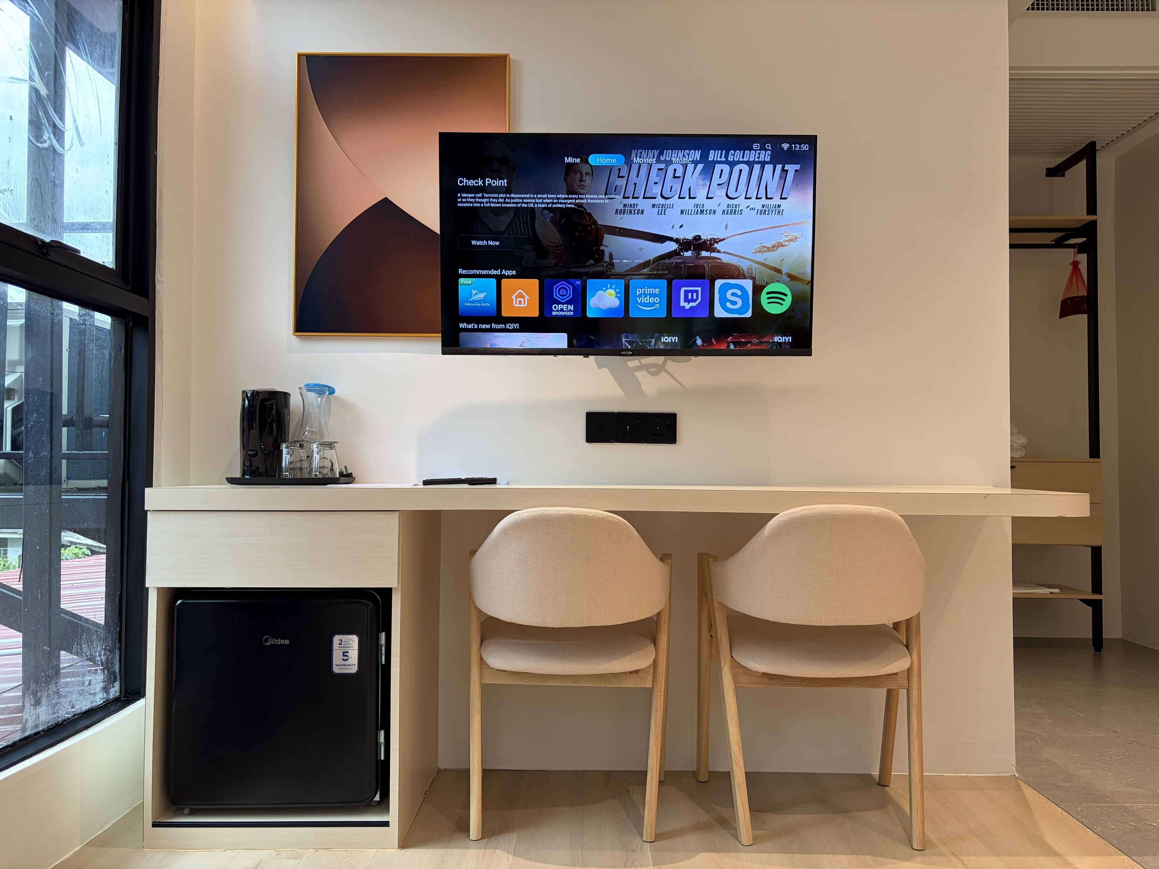 Quarto de hotel moderno com uma televisão de tela plana grande fixada na parede, um minibar compacto, duas poltronas acolchoadas e uma geladeira pequena.