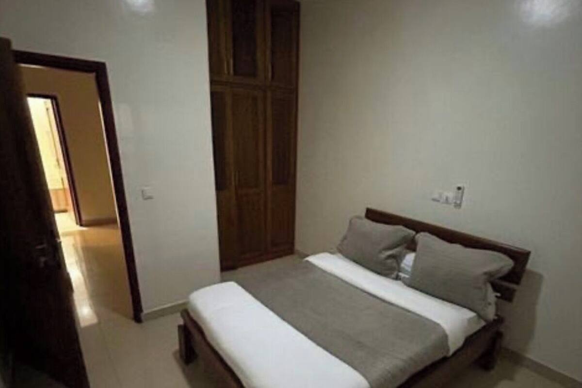 Quarto com uma cama, um guarda-roupa de madeira e uma porta que dá para outro espaço.