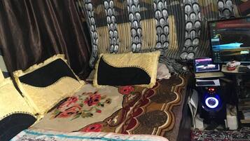 Quarto com cama, um laptop sobre uma mesinha de apoio e um computador de mesa com luz azul.