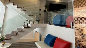 Interior moderno com escada que dá para um andar superior, área de estar com sofá e almofadas, e televisão fixada na parede.