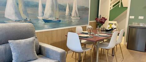 Uma sala de estar moderna com um sofá cinzento, mesa de jantar com cadeiras e um quadro de veleiros na parede.