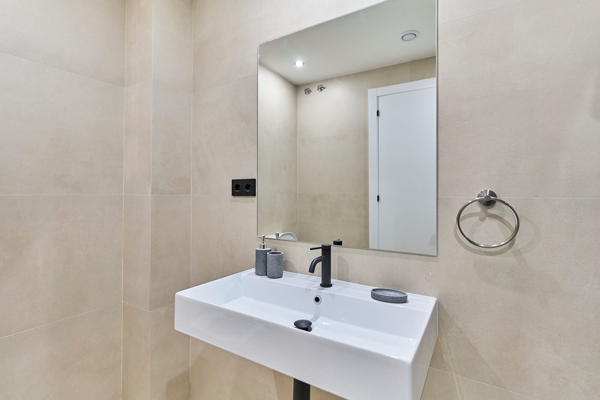Uma casa de banho moderna com lavatório branco, espelho e suporte para toalhas.