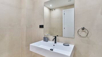 Uma casa de banho moderna com lavatório branco, espelho e suporte para toalhas.
