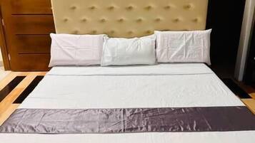 Uma cama com cabeceira estofada, roupa de cama branca e chão de madeira.
