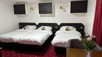 Quarto de hotel com duas camas, um tapete vermelho, uma mesa de madeira e um vaso com flores.