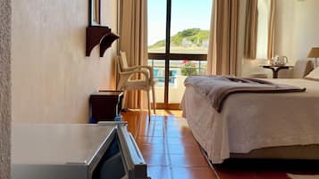 Quarto de hotel com cama, escrivaninha, cadeira, televisão e varanda com vista para as colinas.