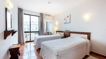 Quarto de hotel com duas camas, varanda com vista, uma mesa pequena e ar-condicionado fixado na parede.