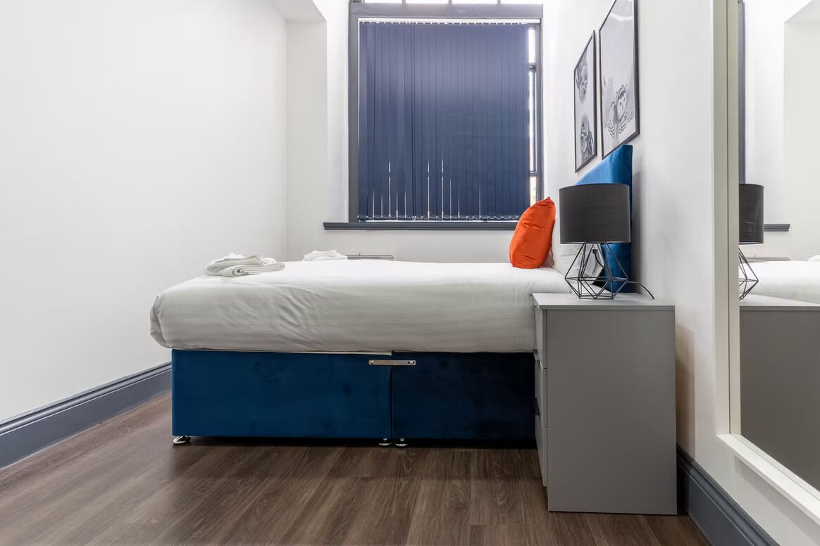 Quarto moderno com cama, mesa de cabeceira, abajur e janela com persianas.