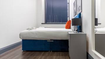 Quarto moderno com cama, mesa de cabeceira, abajur e janela com persianas.