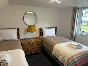 Quarto de hotel com duas camas, mesa de cabeceira, abajur, espelho e janela com vista para o exterior.